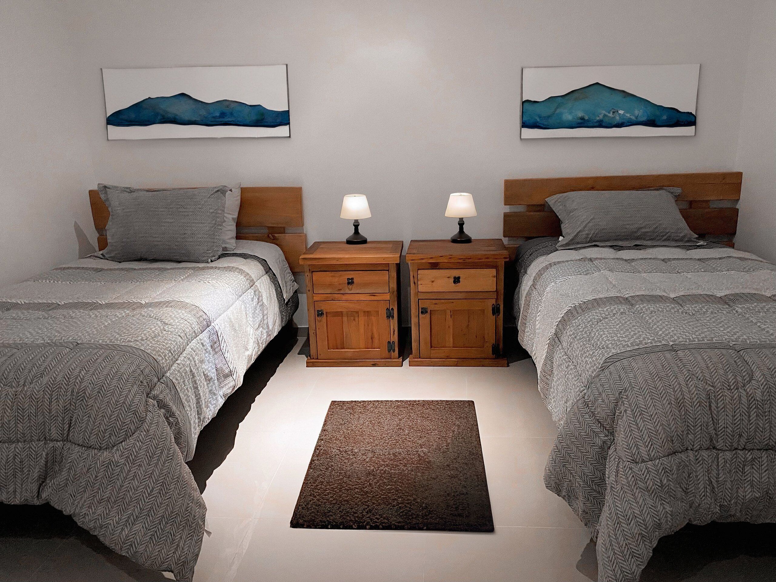 Quarto duplo com duas camas, mesas de cabeceira, tapete e obras de arte na parede.