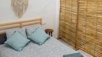 Quarto com cama, ventilador de teto, um pendente de macramé, um divisório de tecido e um banquinho.