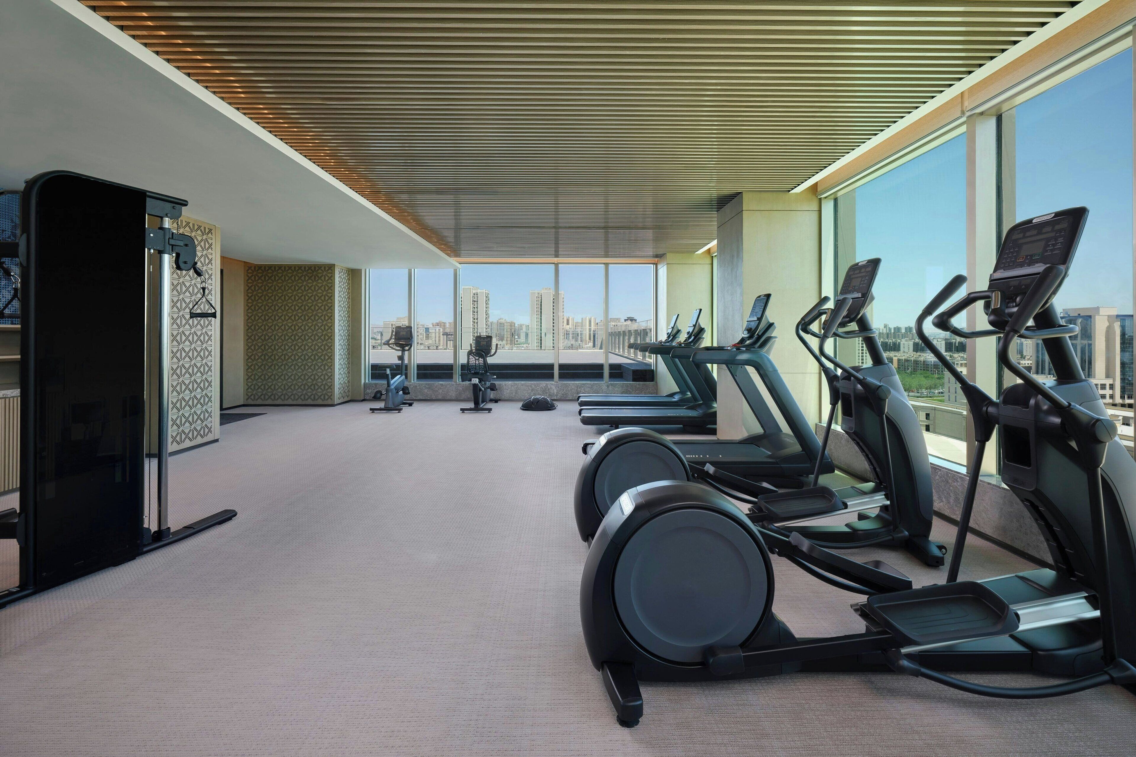 Uma academia moderna com esteiras, um banco de musculação e uma grande janela com vista para a cidade.