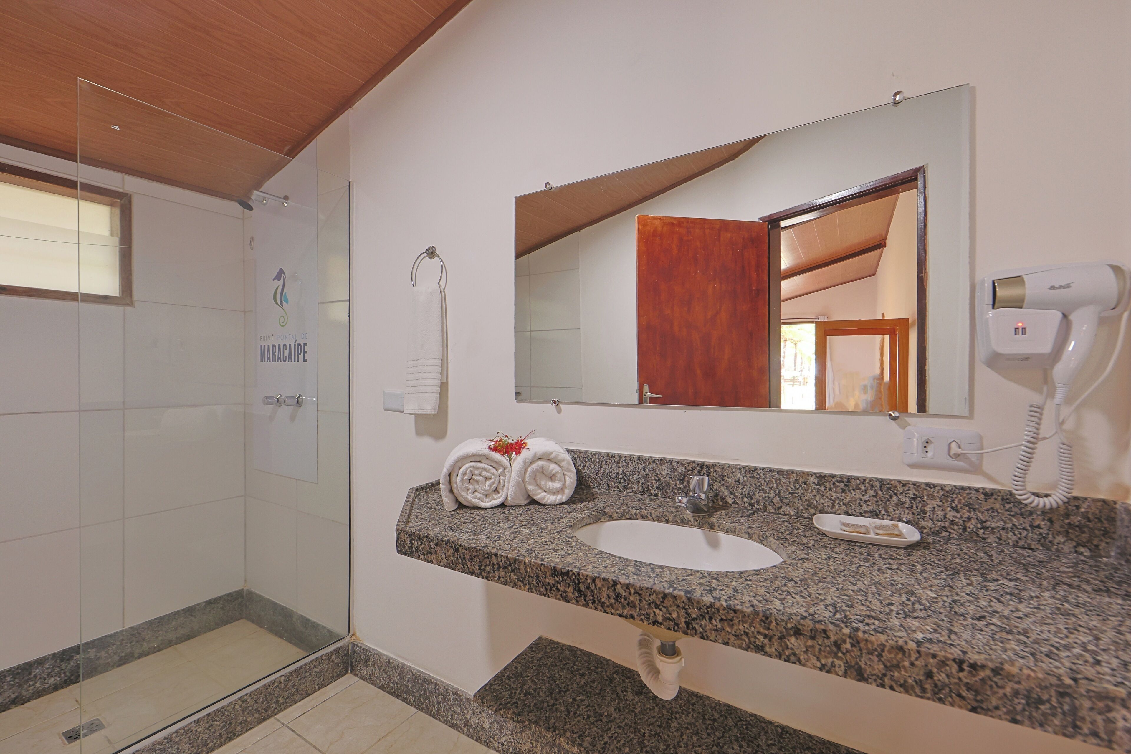 Casa de banho com cabine de chuveiro em vidro, lavatório com bancada de granito, espelho e secador de cabelo.