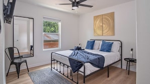 Quarto com cama, ventilador de teto, TV fixada na parede, janela e porta.