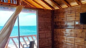 Quarto com cama, vista para a praia e teto de madeira.