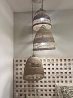 Um quarto com luminária pendente de fibra trançada e painel de parede de madeira treliçada.