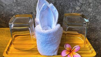 Uma bandeja de madeira com duas garrafas de vidro transparente e uma toalha branca com uma flor rosa.