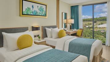 Quarto de hotel com duas camas, uma secretária, uma cadeira, uma janela grande com vista para áreas verdes e uma obra de arte de cavalo-marinho emoldurada na parede.