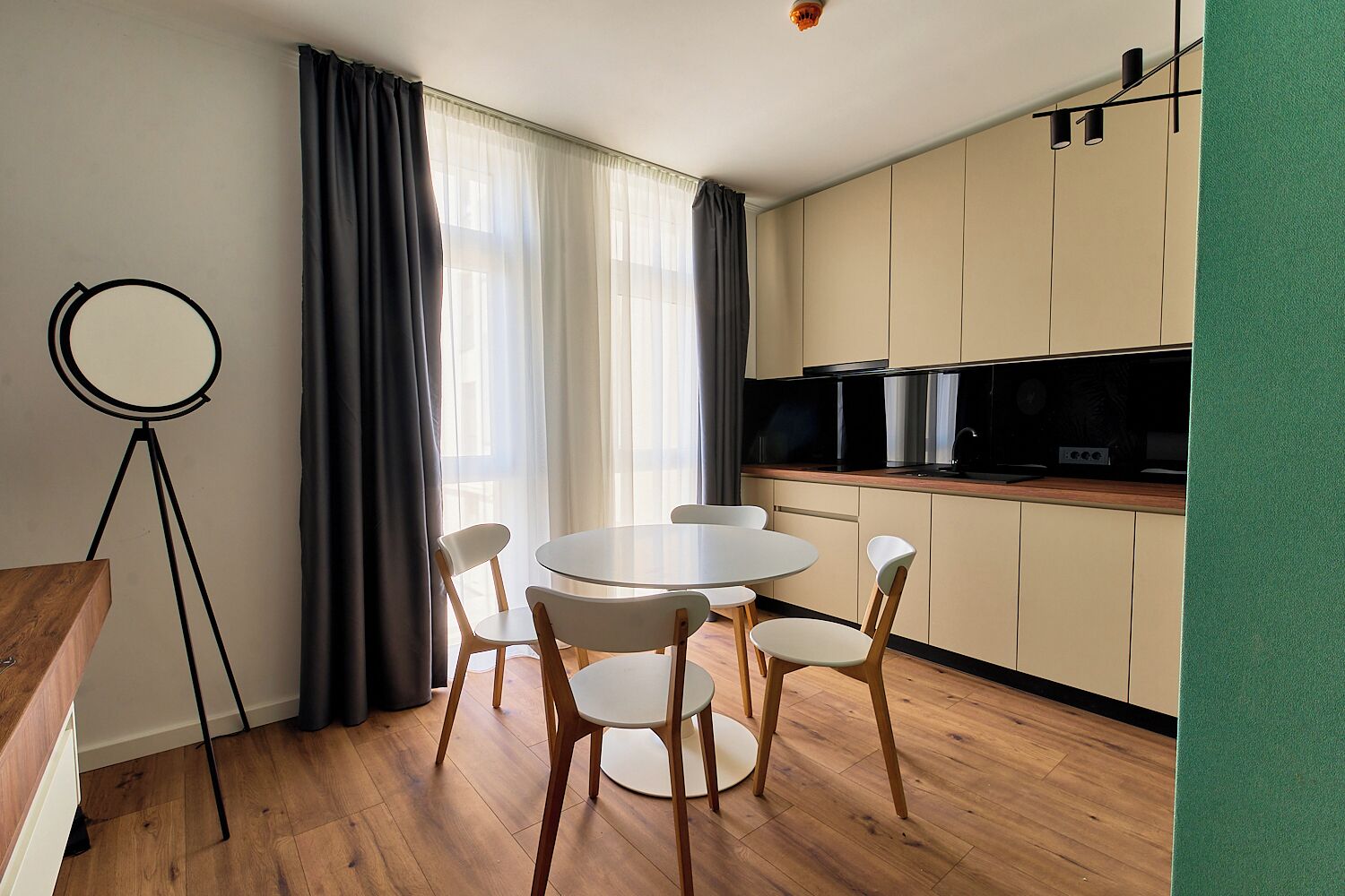 Uma cozinha compacta com uma mesa redonda e cadeiras, um tripé e uma janela grande com cortinas.