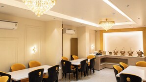 Uma sala de jantar com mesas, cadeiras, um candelabro e uma exposição de objetos decorativos.
