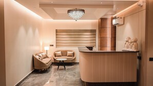 Um lobby moderno com um balcão de recepção, dois sofás, um candelabro e um ar condicionado fixado na parede.