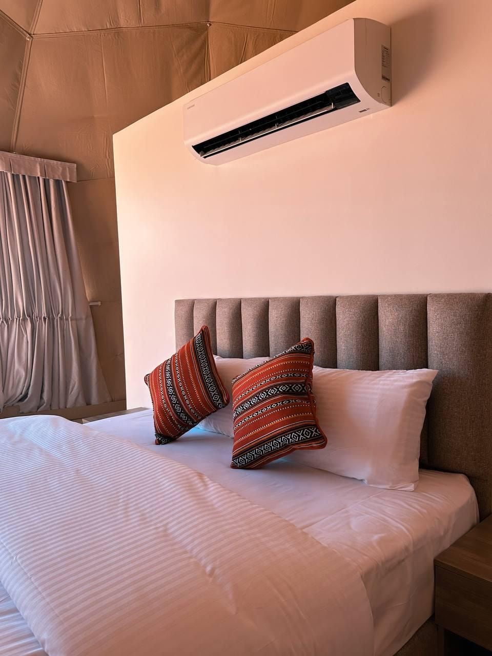 Quarto de hotel com uma cama, almofadas, mesa de cabeceira e ar condicionado fixado na parede.