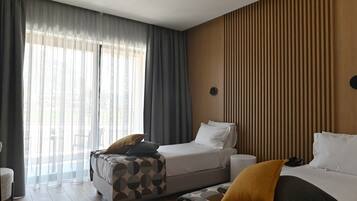 Quarto de hotel com duas camas, um sofá, uma mesa pequena e uma janela com cortinas.