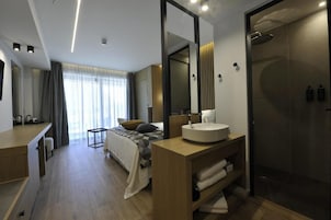 Quarto de hotel moderno com uma cama grande, toucador com espelho, área de chuveiro e vista para o exterior.