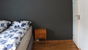 Quarto com cama, mesa de cabeceira, piso de madeira e ventoinha no teto.