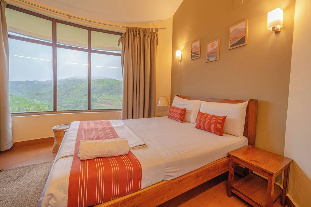 Quarto com uma cama grande, mesa de cabeceira, janela com cortinas e luminárias fixadas na parede.