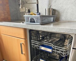Cozinha com máquina de lavar louça, pia com torneira e dispensador de sabão.