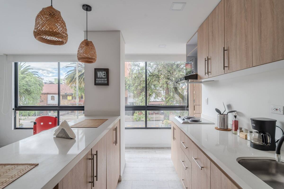 Uma cozinha moderna com armários de madeira, bancada branca e uma grande janela com vista para a rua.