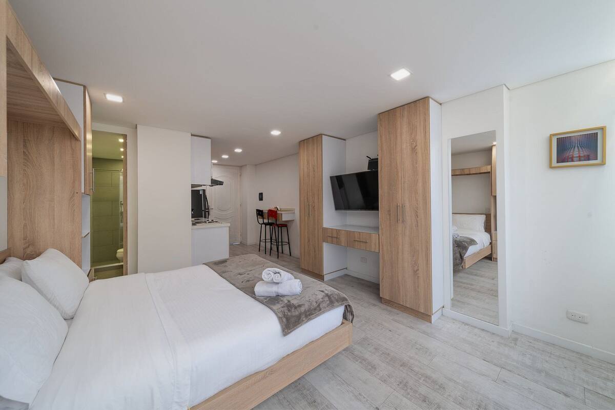 Quarto de hotel moderno com uma cama grande, escrivaninha, televisão e espelho.