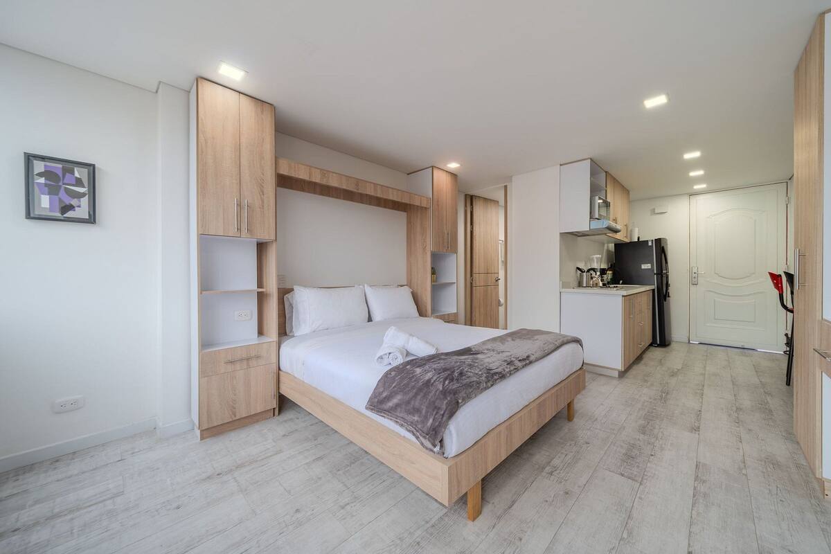 Quarto moderno com cama de madeira, estantes embutidas e uma kitchenette.