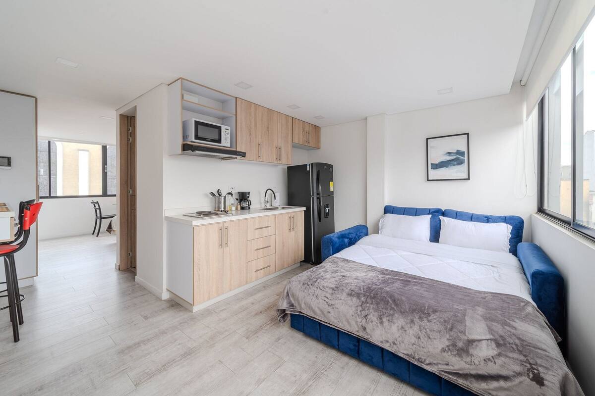 Quarto moderno com cama grande, roupeiro embutido, kitchenette e janela que traz luz natural.