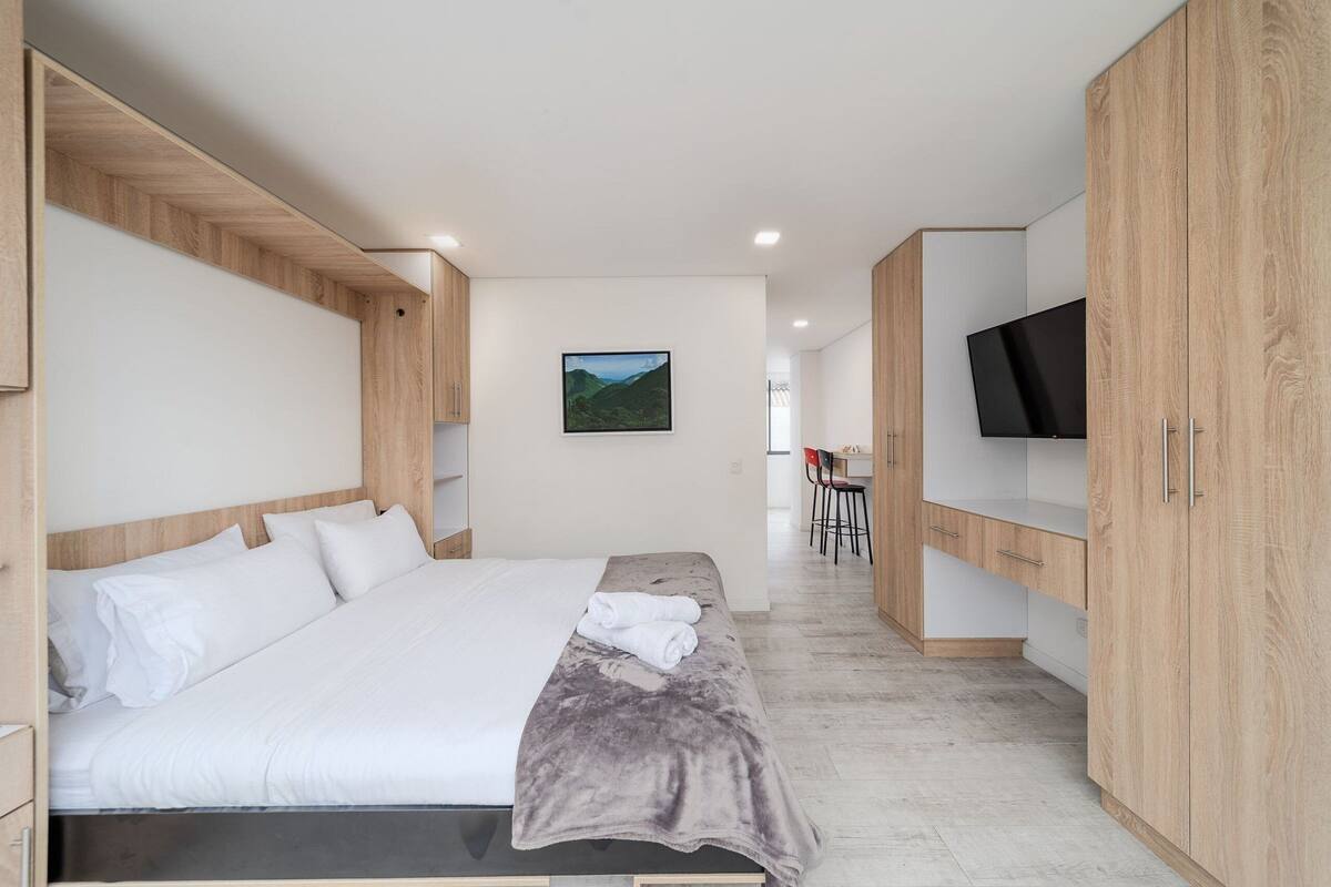 Quarto de hotel moderno com uma cama grande, guarda-roupa de madeira e televisão de tela plana.