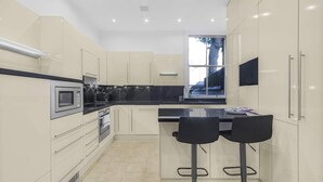 Cozinha moderna com armários brancos, bancada preta e dois banquetes pretos.