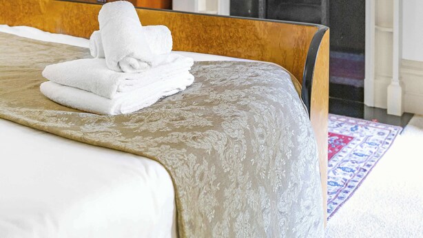 Uma cama bem arrumada com uma toalha dobrada, um penteado de madeira, uma lareira branca e um espelho grande e ornamentado.