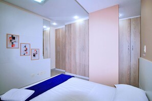 Quarto com cama, colcha azul, armários de madeira e quadros nas paredes.