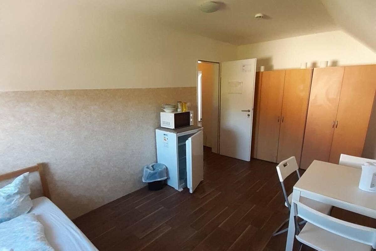 Quarto compacto com cama, pequeno espaço de cozinha, mesa de jantar com cadeiras e um guarda-roupa.