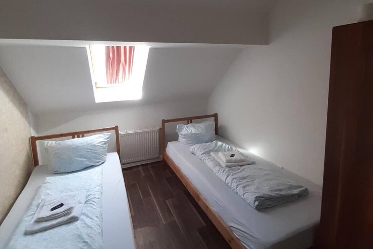 Um apartamento pequeno e compacto, com um quarto e duas camas individuais, piso de madeira, teto inclinado e janela no teto com cortinas.