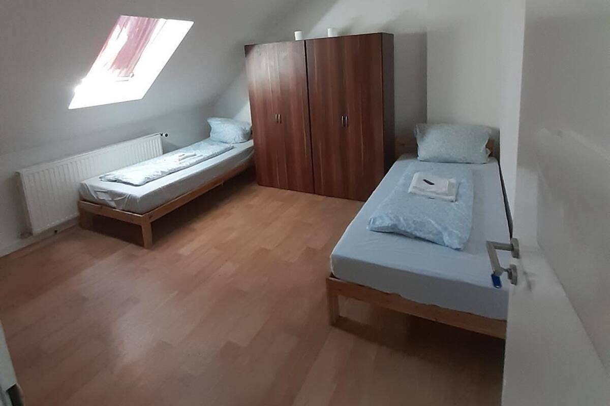 Um pequeno apartamento de um quarto, com duas camas, um guarda-roupa e um claraboia.