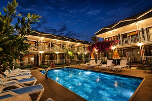 Um hotel com piscina, espreguiçadeiras e varanda com plantas.