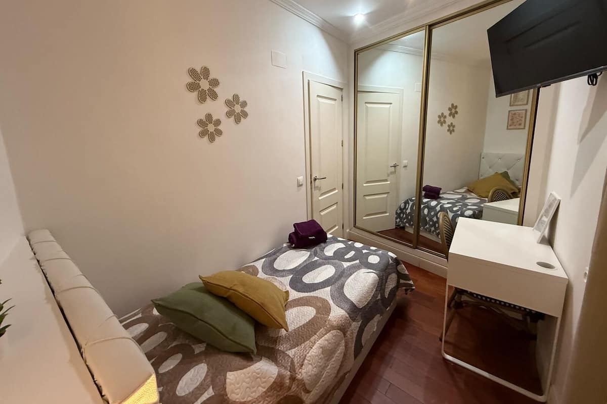 Quarto com cama, guarda-roupa, espelho e escrivaninha.