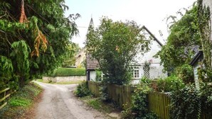 Uma estrada rural estreita que leva a uma casa branca com telhado de palha.