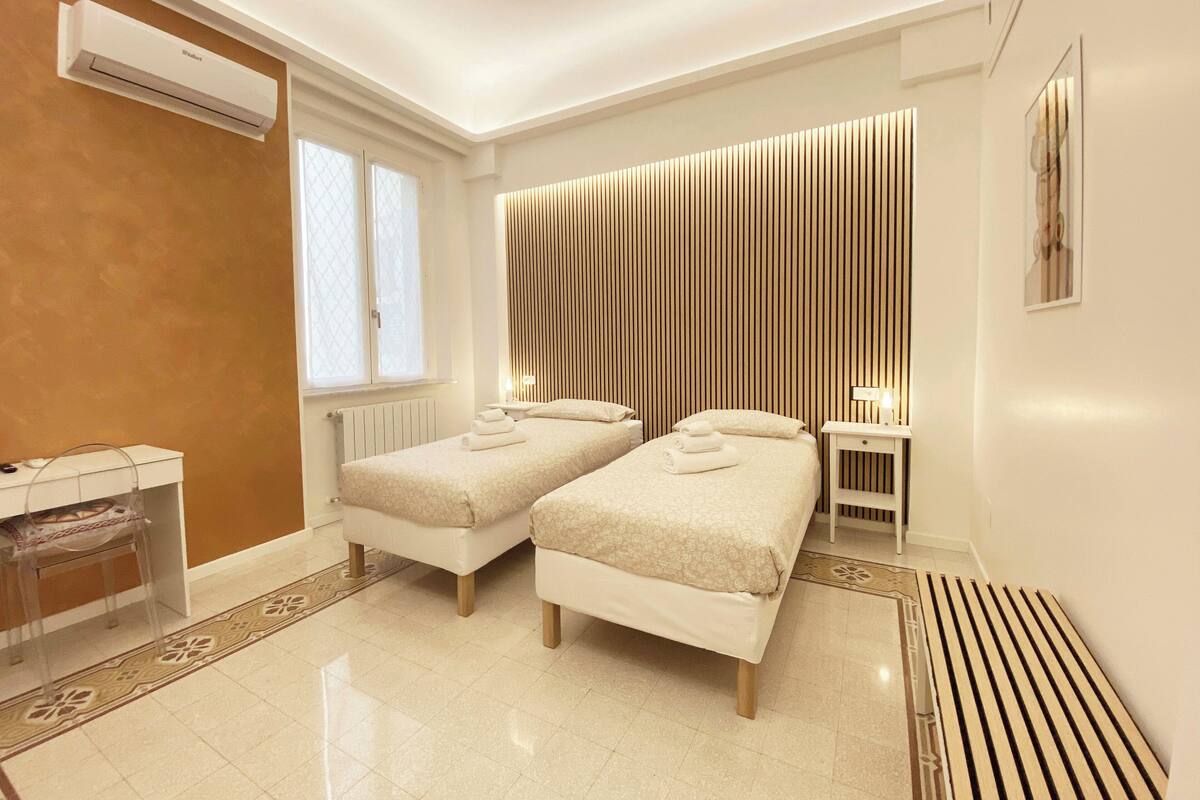 Quarto de hotel moderno com duas camas, um radiador, uma janela e um ar condicionado fixado na parede.