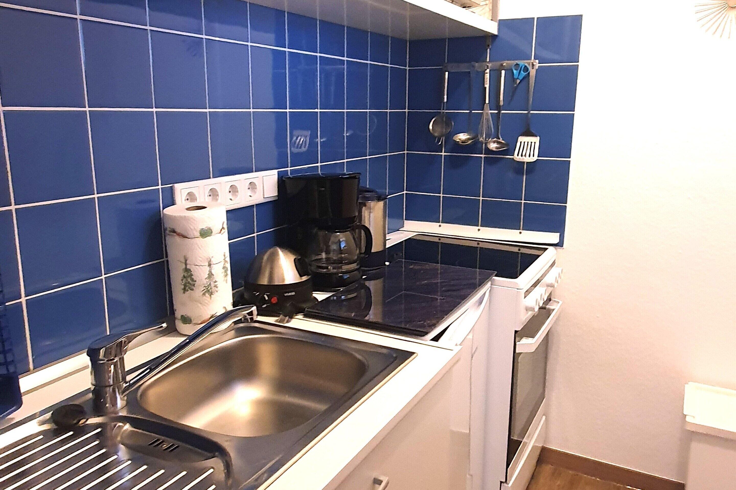 Cozinha compacta com azulejos azuis, pia de aço inoxidável, cafeteira e fogão.
