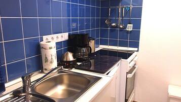 Cozinha compacta com azulejos azuis, pia de aço inoxidável, cafeteira e fogão.