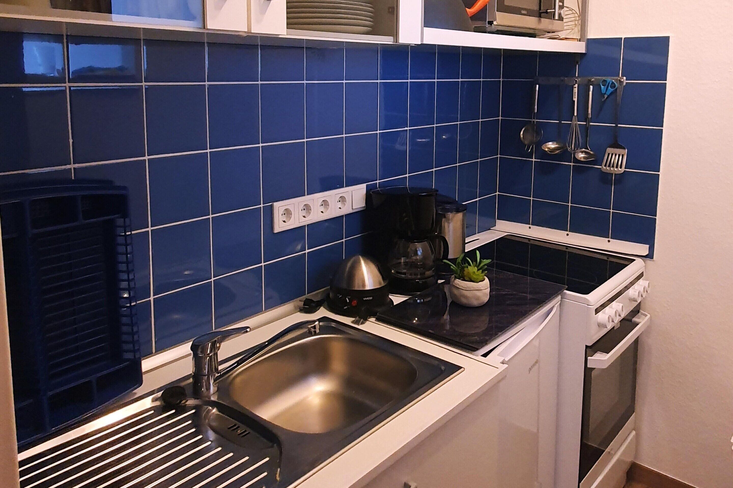 Cozinha compacta com azulejos azuis, uma pia de aço inoxidável, cafeteira e fogão.