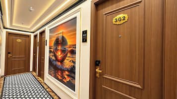 Corredor de hotel com portas de madeira, com os números 302 e 308, e uma grande obra de arte emoldurada retratando um globo em chamas.