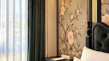 Quarto de hotel com cama, mesa de cabeceira, parede com papel de parede floral e janela com cortinas.