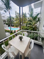 Varanda com mesa e cadeiras, vista para uma piscina e vegetação exuberante.