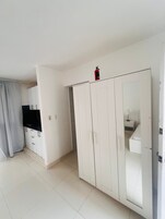 Quarto com guarda-roupa, cama, mesa de cabeceira e janela com cortina.