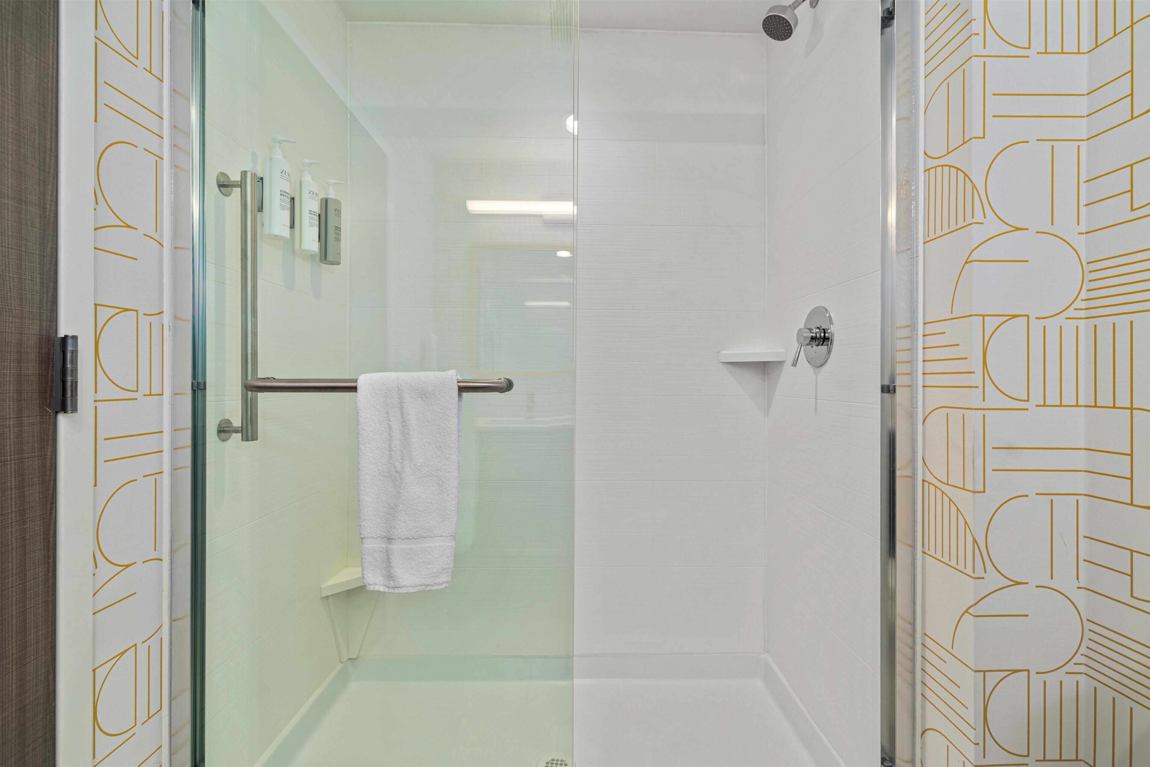 Um chuveiro envidraçado com uma toalha branca em um porta-toalhas, uma porta de vidro e um design de parede padronizado.