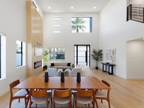 Uma sala de estar espaçosa com uma grande mesa de jantar de madeira, assentos confortáveis e vista para o exterior através de amplas janelas.