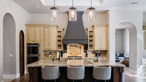 Uma cozinha moderna com ilha central, banquetas e iluminação pendente.