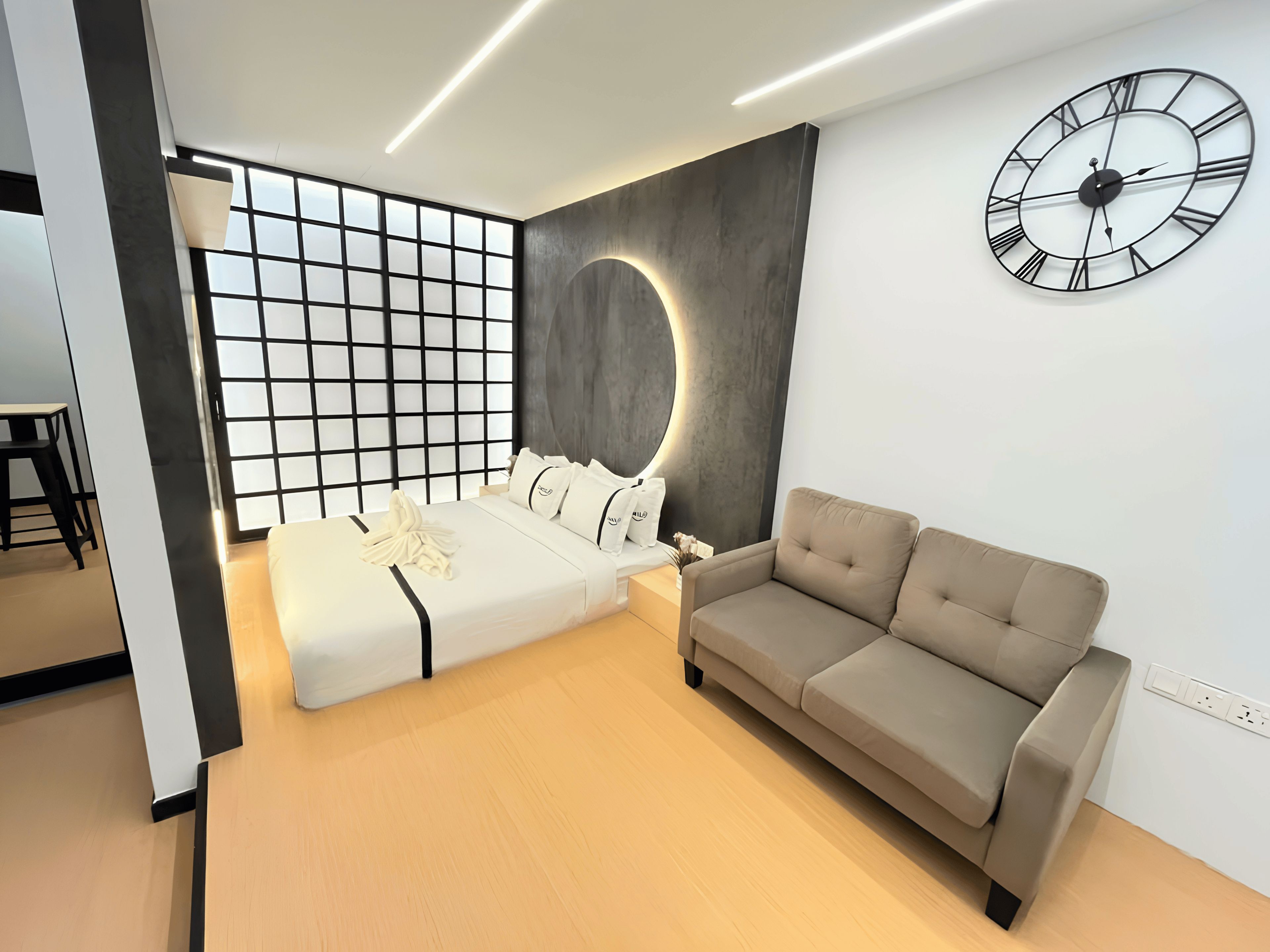 Quarto moderno com cama, sofá, relógio de parede e painel decorativo.