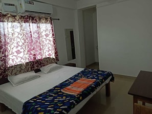 Quarto com cama, mesa e janela com cortinas.