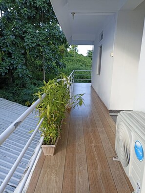 Uma varanda com piso de madeira, grade branca e unidade de ar condicionado branca.