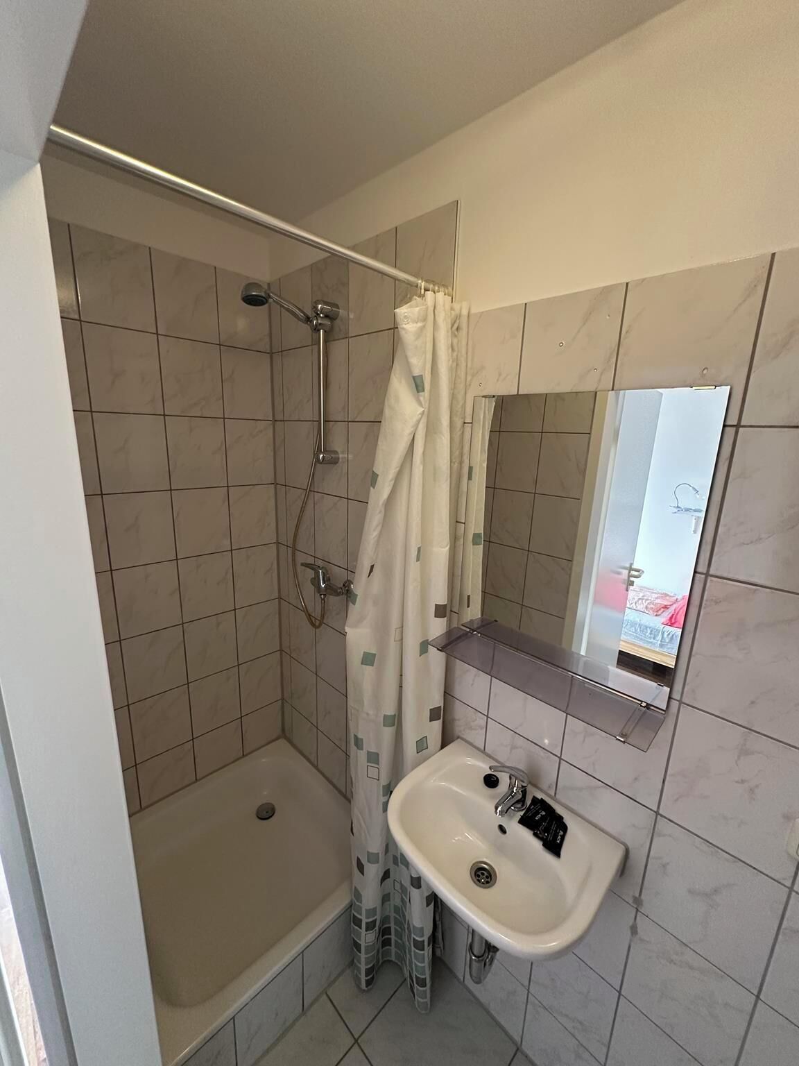 Um banheiro pequeno com azulejos, chuveiro, pia e espelho.