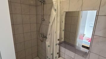 Um banheiro pequeno com azulejos, chuveiro, pia e espelho.