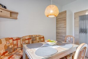 Uma área de jantar com mesa de vidro, luminária pendente de fibra, sofá estampado e uma tigela de frutas.