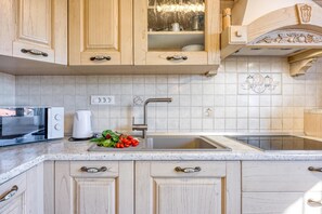 Cozinha com armários de madeira, pia de aço inoxidável e bancada com chaleira e frutas frescas.